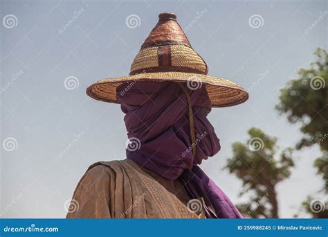Fulani Man In Traditional Clothing With Wide Hat Sitting On His White