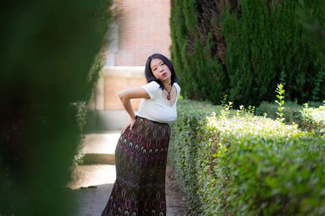 젊고 행복하고 아름다운 아시아 한국 여성이 임신 한 도시 공원에서 야외에서 행복하고 쾌활한 포즈를 취하고 임신과 출산 개념에 미소를 짓는 배꼽을 보여줍니다 30 34세에