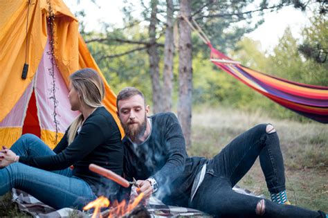 아름 다운 커플 앉아 캠프 파이어 주위에 캠핑 텐트와 배경에 남자 막대기로 화재 제스처 건강한 생활방식에 대한 스톡 사진 및 기타 이미지 Istock