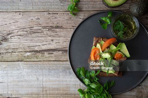 어두운 호 밀 토스트 빵에 건강 한 아보카도 샌드위치 신선한 슬라이스 아보카도 씨앗과 소박한 나무 배경에 토마토로 만든 공간에 복사 합니다 0명에 대한 스톡 사진 및 기타