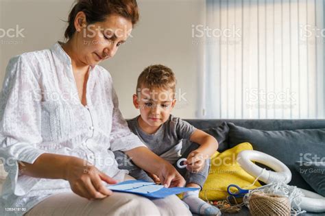 하루 에 소파에 그의 어머니에 앉아 작은 소년 장식 여자는 아파트에서 소파에 예술 제품을 만들기 위해 그녀의 아들을 가르친다 집에서 일하는 성숙한 여성 디자이너 국내 생활