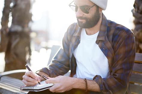 암기 화창한 봄 날씨를 즐기고 취미에 시간을 보내는 그의 여행에 대 한 크리에이 티브 파란색된 남성 관광 만드는 여행 노트 드로잉 벤치에 앉아 Hipster 남자 메모장