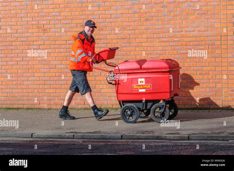 Royal Mail Postman Dressed In His Uniform Wearing Shorts Pushing A