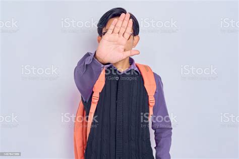 배낭을 메고 캐주얼한 옷을 입은 진지한 젊은 아시아 학생 남자가 회색 배경에 고립된 열린 손바닥으로 얼굴을 가리고 제스처를 멈춥니다 고등학교 대학 대학 개념 30 34세에