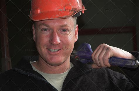 عکس کارگر خندان با لباس کار و کلاه ایمنی و ابزار کار در محل کار عکس با کیفیت و تصاویر استوک