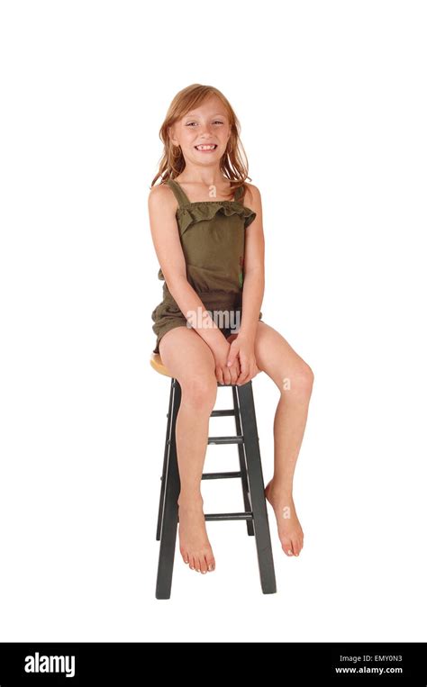 A Young Smiling Blond Girl In A Olive Green Jumpsuit Sitting In A Bare