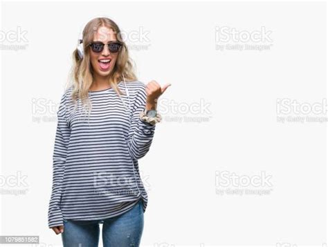 아름 다운 젊은 금발 여자 생기고 엄지 측면 가리키는 행복 한 얼굴로 웃 고 고립 된 배경 위에 헤드폰 선글라스를 착용 가리키기에 대한 스톡 사진 및 기타 이미지 Istock