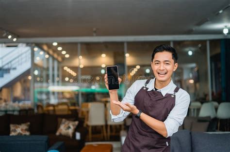 Male Shop Assistant With Hand Gesture Presenting Mobile Phone In Furniture Store Stock Image Male Shop Assistant With Hand Gesture Presenting Mobile Phone In Furniture Store Stock Image