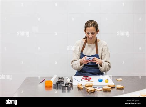 Female Pastry Chef Using Her Mobile Phone While Working In The Kitchen