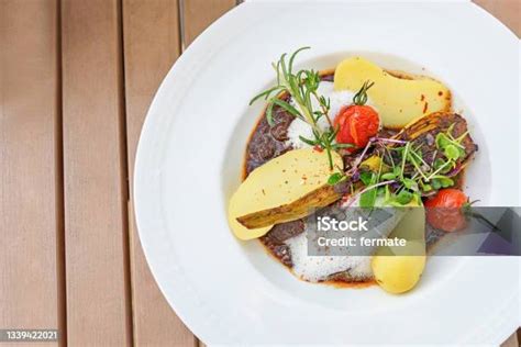 감자 토마토 구운 회향 크레스 허브 콩나물의 장식을 곁들인 소고기 스튜는 나무 테이블에 흰색 접시에 장식폼과 함께 제공되며 복사 공간 위에서 바라보는 높은 각도의 전망