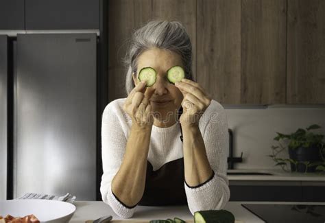 Senior Woman Having Fun With Cucumber Slices In Kitchen Stock Image