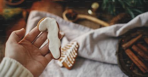 냅킨 양초 장식이 있는 소박한 테이블의 배경에 장식된 진저브레드 쿠키 사탕 지팡이를 들고 있습니다 무디 이미지 세련된 크리스마스 진저 브레드 쿠키를 만드는 여자 사진