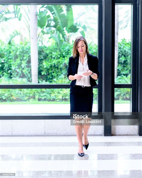 50대 중반의 전문직 여성이 사무실에서 태블릿을 들고 이동 중에도 일하고 있다 50 54세에 대한 스톡 사진 및 기타 이미지 50 54세 경영자 고용과 노동 Istock