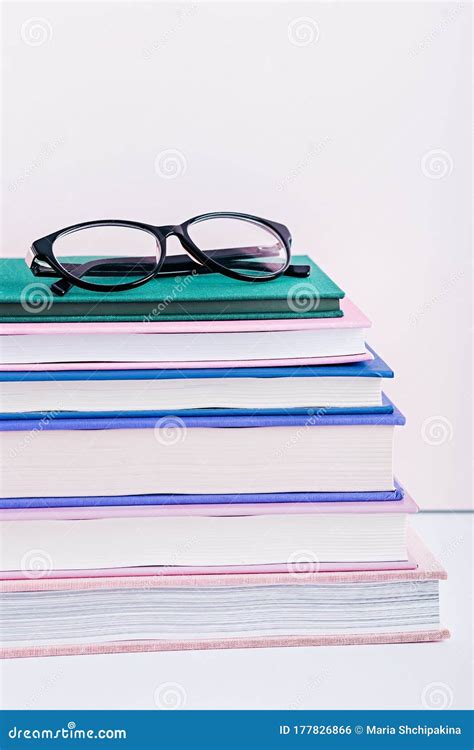 Stack Of Books On Bookshelf With Reading Glasses Against Pink Wall
