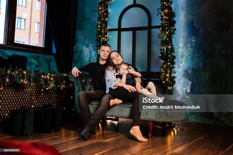 메리 크리스마스와 해피 홀리데이 아빠 엄마와 어린 딸은 집에서 크리스마스 장식 근처에서 키스하고 포옹하고 즐겁게하고 있습니다 장식 된 객실 인테리어에 선물과 함께 행복한