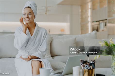 사람들의 아름다움과 스킨 케어 컨셉 만족한 여성 용 페이스 크림을 적용 얼굴 트리트먼트를 즐긴다 미소 옆으로 미소 부드럽게 사용