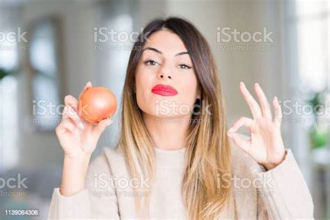 집에서 신선한 양파를 들고 젊은 아름 다운 여 자가 손가락으로 확인 표시 우수한 기호 갈색 머리에 대한 스톡 사진 및 기타