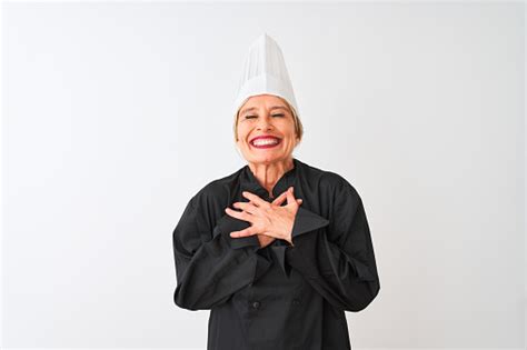 유니폼과 모자를 쓰고 고립된 흰색 배경 위에 서있는 중년 요리사 여성은 닫힌 눈과 얼굴에 감사하는 제스처로 가슴에 손을 대고