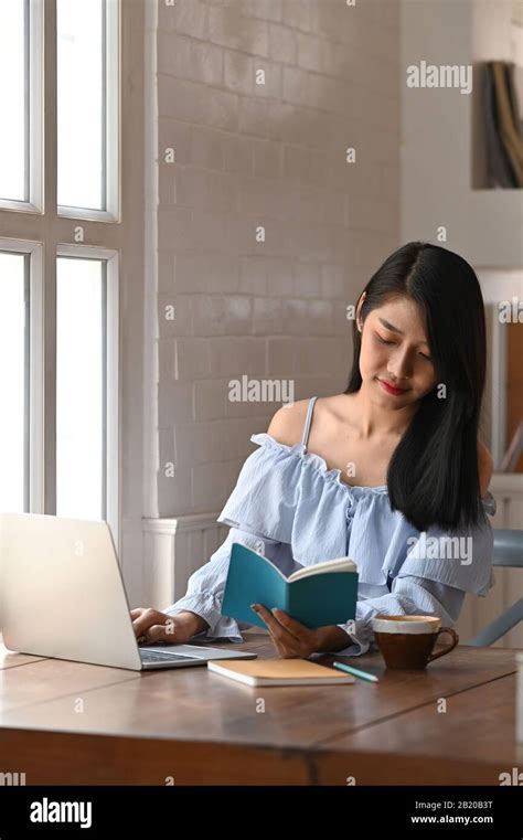 Beautiful Woman Reading A Book While Sitting In Front A Computer Laptop