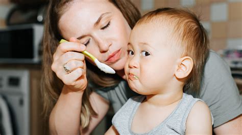 모성 베이비 케어 어린이를위한 건강 식품 개념 숟가락을 든 엄마는 집에서 부엌에 앉아있는 동안 아기에게 먹이를줍니다 아이가 먹고 어머니와 함께 아침 식사를하고 카메라를 재미