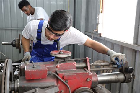 금속 선반 기계를 사용하여 보호 유니폼을 입은 다민족 기술자 또는 노동자는 차고에서 자동차 디스크 브레이크 연마를 작동합니다