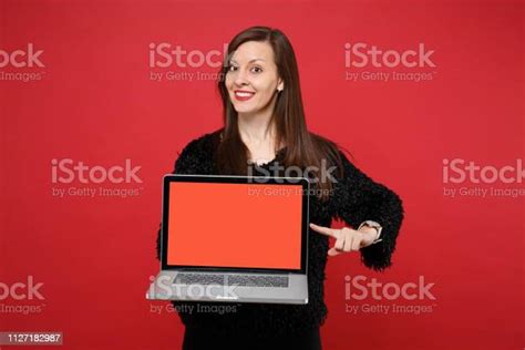 노트북 Pc 컴퓨터 빨간색 배경에 고립 된 빈 빈 화면에 검은 모피 스웨터 포인팅 검지 손가락에 아주 젊은 여자 사람들이 진심으 감정 라이프 스타일 개념 복사 공간을 비웃는