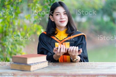 대학 캠퍼스에서 공부하는 학술 가운을 입은 젊은 명랑한 아름다운 여성 졸업생이 책과 책과 나래를 테이블에 놓습니다 공부에 대한 스톡 사진 및 기타 이미지 Istock