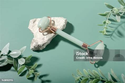 녹색 옥 돌 롤러 얼굴 마사지 구아샤는 녹색 가지가 있는 녹색 배경에 돌무더기 돌무더기 위에 있습니다 얼굴 치료 및 홈 스파 노화 방지 피부 관리 천연 유기농 미용 제품 0