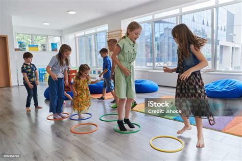 작은 보육원 아이들 교실에서 실내 바닥에 여성 교사와 함께 운동을하고 훌라 후프 서클을 뛰어 넘으면 바닥에서 추적됩니다 Mental Wellbeing에 대한 스톡 사진 및