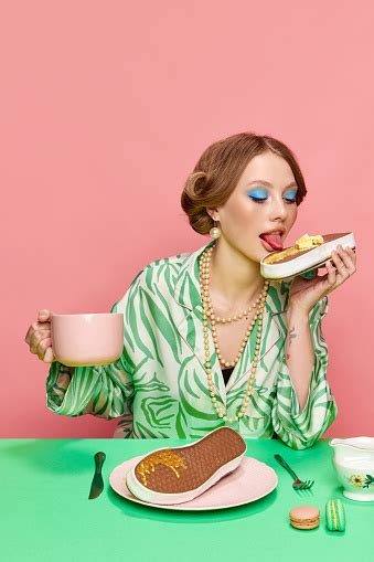 분홍색 스튜디오 배경에 버터를 바른 스니커즈 와플에서 꿀을 핥는 아름다운 어린 소녀 아침 식사와 커피 1970 1979 년에