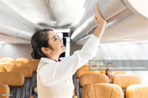 아시아 여성 승무원이 승객이 앉은 후 수하물 운반을 위해 오버 헤드 수하물 칸 뚜껑을 닫고 이륙 준비를합니다 승무원 교통 관련 직업에 대한 스톡 사진 및 기타 이미지