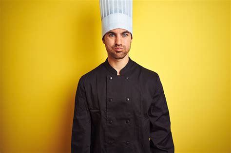 재미 있는 얼굴과 고립 된 노란색 배경 퍼핑 뺨 위에 서 유니폼과 모자를 입고 젊은 요리사 남자 공기 미친 표정으로 입이 팽창 사진 이미지에 대한 스톡 사진 및 기타 이미지