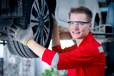 빨간 제복을 입은 미소 짓는 잘 생긴 정비공은 들어 올린 차량 차고에서 바퀴를 점검하는 자동차 정비사 수리 서비스 상점에서