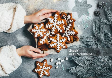 크리스마스 글레이즈 진저 브레드 쿠키와 눈송이와 계피 스틱의 형태로 크리스마스 트리와 새해 화환으로 장식 된 회색 배경에 여성의 손에 스틱 손수 만든에 대한 스톡 사진 및