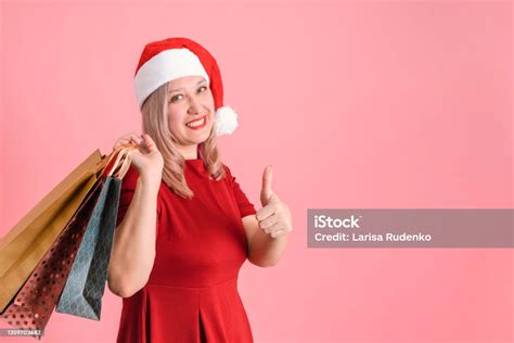 분홍색 배경에 선물 가방을 가진 산타 모자를 쓴 한 여성이 엄지 손가락을 들고 제스처를 보여줍니다 35 39세에 대한 스톡 사진 및 기타 이미지 Istock