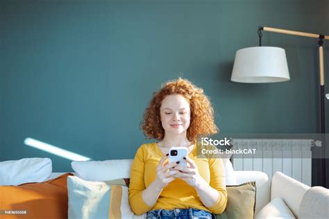 거실에서 스마트폰을 사용하는 아름 다운 빨간 머리 여자 30 34세에 대한 스톡 사진 및 기타 이미지 30 34세 Brand Name Online Messaging