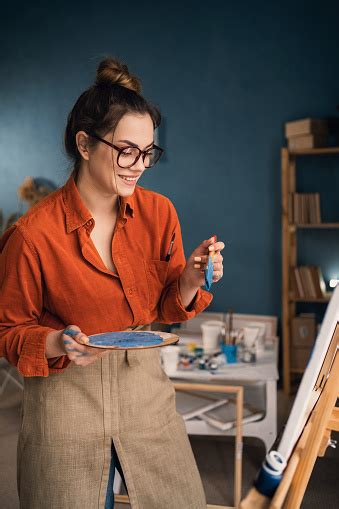 캐주얼 옷을 입은 소수 민족 여성은 캔버스 근처에 서서 손에 물감이 든 팔레트를 들고 캔버스를 바라보며 새로운 그림을 만드는 것에 대해 생각합니다 취미와 휴가 개념 여자에