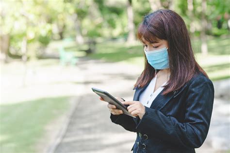 스마트 폰 태블릿을 사용하여 얼굴 마스크를 착용 하는 비즈니스 여성 일출 및 흐림 자연 배경 공원에서 응용 프로그램 장치와 함께 작동 하는 화면에 입력 코로나 바이러스 또는