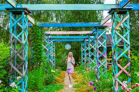 빨간 배낭을 등에 메고 있는 니트 스웨터를 입은 어린 금발 소녀가 손에 든 전화가 공원이나 숲의 나무 색 아치의 길을 따라 걷고