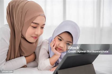 무슬림 아시아 어린이 소녀와 그녀의 어머니는 흰색 침실에서 침대에 태블릿에서 기술 비디오를 참조하십시오 휴식 행복한 아랍 딸과 엄마는 실내 엔터테인먼트태블릿을보고 히잡을