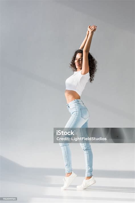 회색 배경에 포즈 청바지에 웃는 곱슬 여자의 전체 길이 보기 갈색 머리에 대한 스톡 사진 및 기타 이미지 갈색 머리 곱슬 머리 미소 Istock