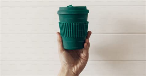 일회용 플라스틱을 금지합니다 흰색 나무 배경에 세련된 재사용 가능한 에코 커피 컵을 들고 있습니다 천연 대나무 섬유로 만든 그린 컵 제로 웨이스트 개념 선택하십시오