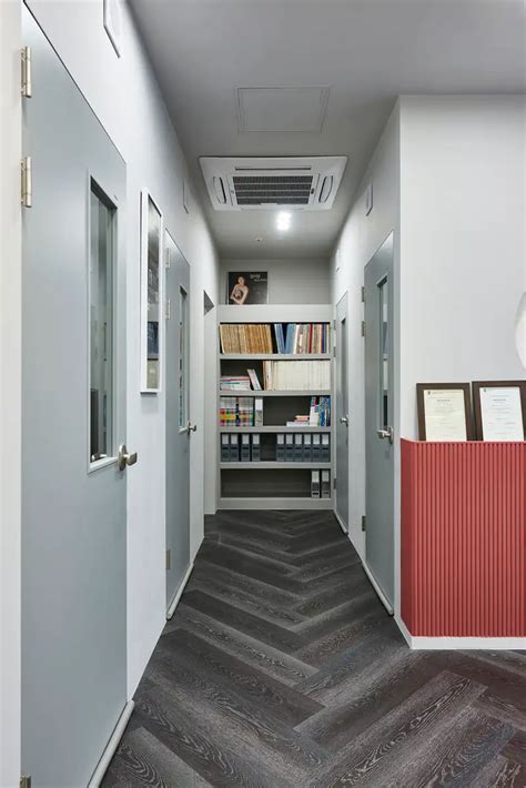 심플 화이트 바탕에 블랙 헤링본 바닥과 긴 창문이 달린 그레이톤 문과 레드 템바보드 포인트 벽이 함께 있는 피아노 학원 복도 공간 사진