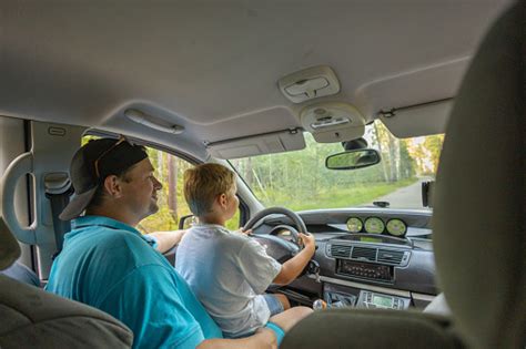 아버지는 아들에게 숲 속의 시골길에서 차를 운전하도록 가르친다 행복한 아이는 아버지의 무릎에 앉아 자동차 운전을 배웁니다 아버지와 아들의 관계에 대한 개념 2명에 대한 스톡