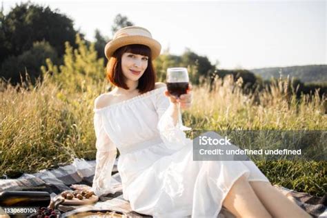 세련된 프로스 드레스 옷 드레스와 모자를 입은 백인 여성 레드 와인 한 잔과 함께 야외에 앉아 녹색에 대한 스톡 사진 및 기타 이미지 Istock