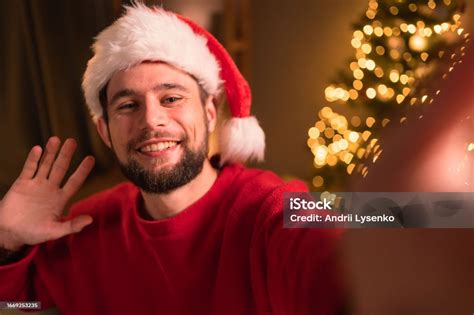 산타클로스 모자를 쓴 행복한 수염 난 남자가 손을 흔들며 셀카를 찍고 영상 통화를 하고 메리 크리스마스 인사를 하거나 브이로그를 촬영한다 크리스마스에 대한 스톡 사진 및