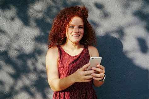 주 근 깨 얼굴 빨간 여름 드레스 회색 콘크리트 벽 배경에 서 있는 동안 휴대 전화의 카메라에 의해 Selfie 복용 입고 매력적인 빨간 머리 Hipster 소녀 여자