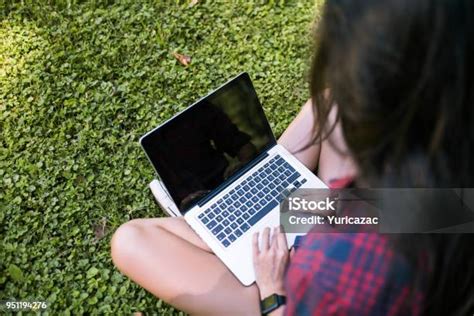 젊은 백인 여자의 노트북 Pc 앞 잔디에 앉아 체크 무늬 셔츠를 입고 무선 통신 그녀의 노트북 컴퓨터에 자른된 상단 후면 보기 쇼핑 하 고 공부 공부에 대한 스톡 사진 및