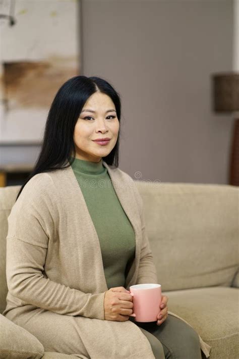 Cute Asian MILF Sitting On Couch With Cup Of Coffee Home The Image Captures Moment Of