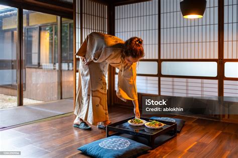 쇼지 슬라이딩 종이 문으로 기모노에 네기 버섯 두부 테이블 플레이트의 볶음 야채를 제공하는 젊은 외국인 여성과 함께 하는 전통적인 일본 집 또는 료칸 방 료칸에 대한 스톡